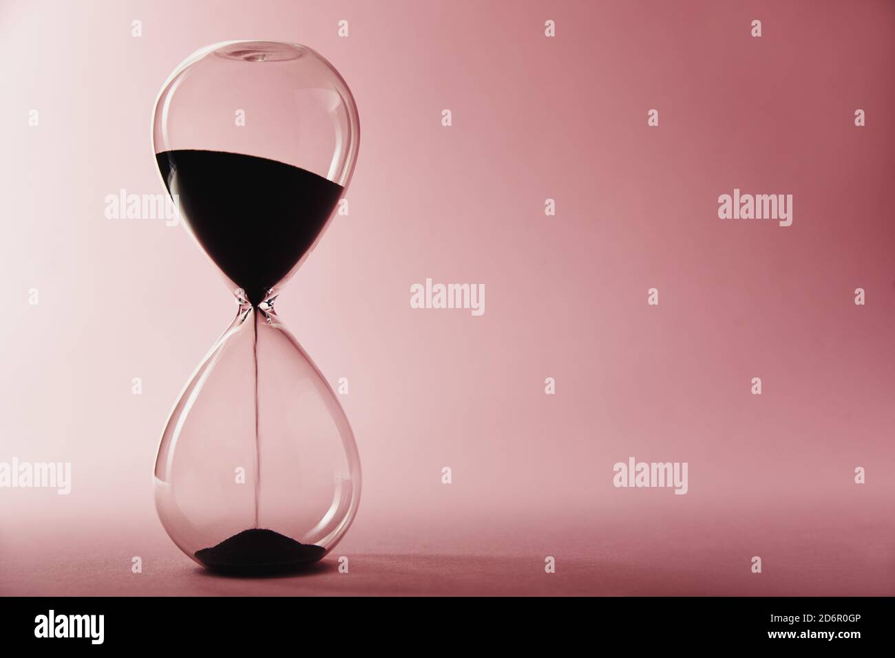Hourglass on pink background, close up. Urgency and running out of time ...