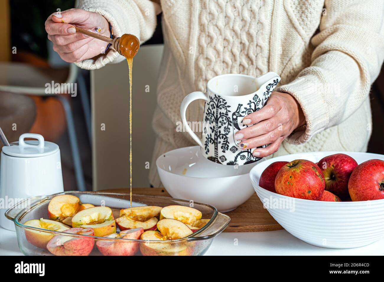 female hands with stick pouring apples with honey in a glass container ...