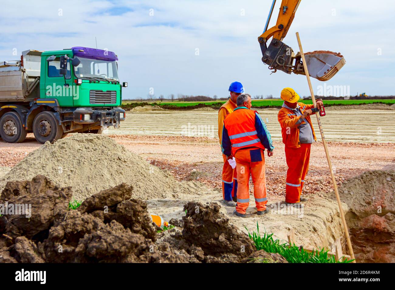 Workers are waiting for excavator to finish digging square trench on ...