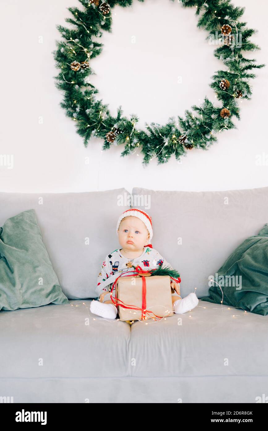 brooding little boy sits in Santa hat and holiday costume on gray sofa ...