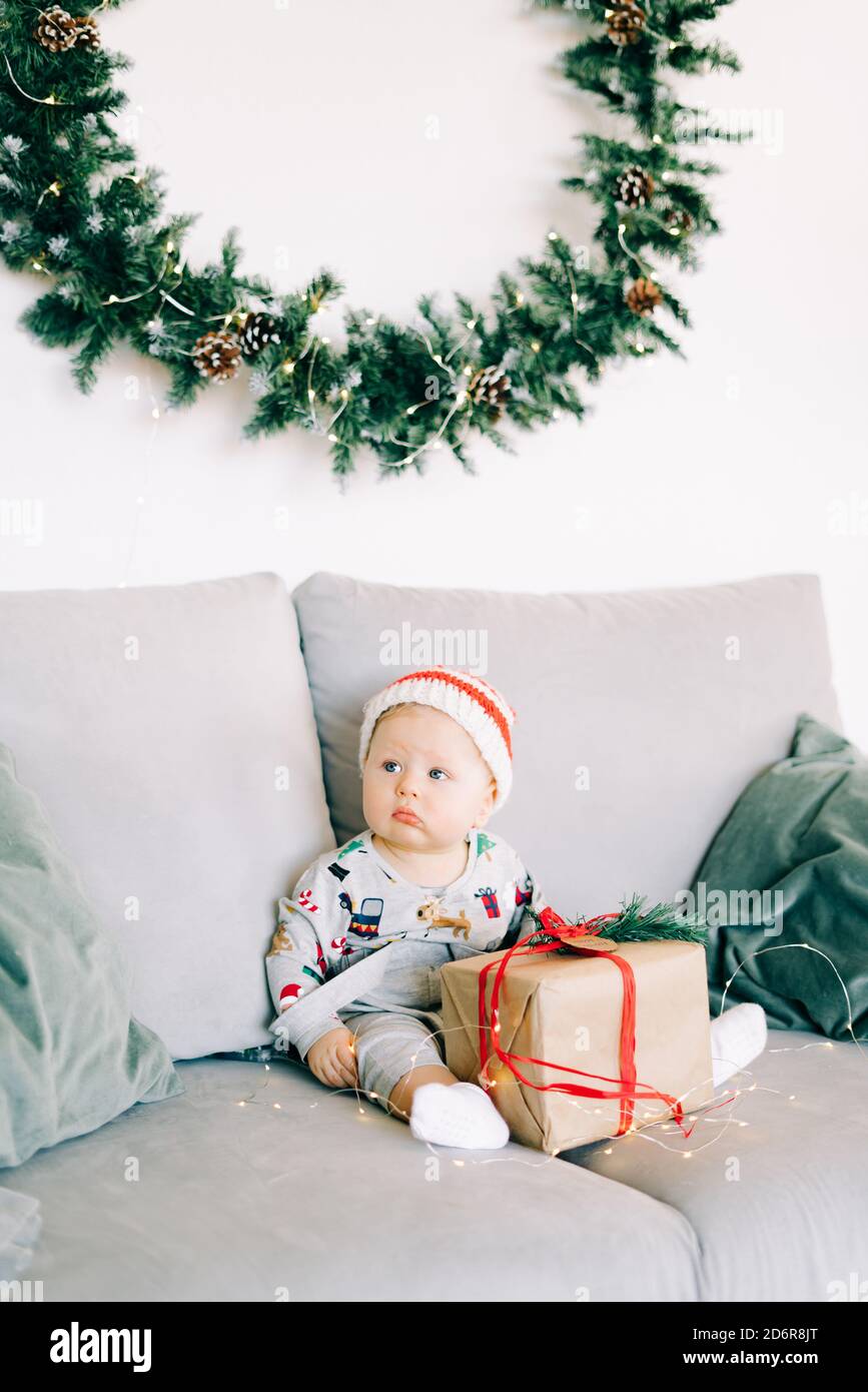 brooding little boy sits in Santa hat and holiday costume on gray sofa ...