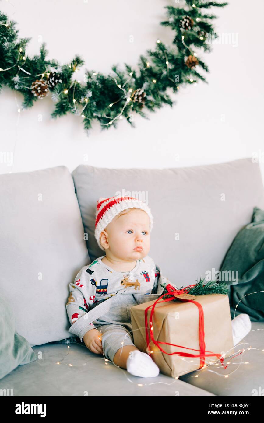 brooding little boy sits in Santa hat and holiday costume on gray sofa ...