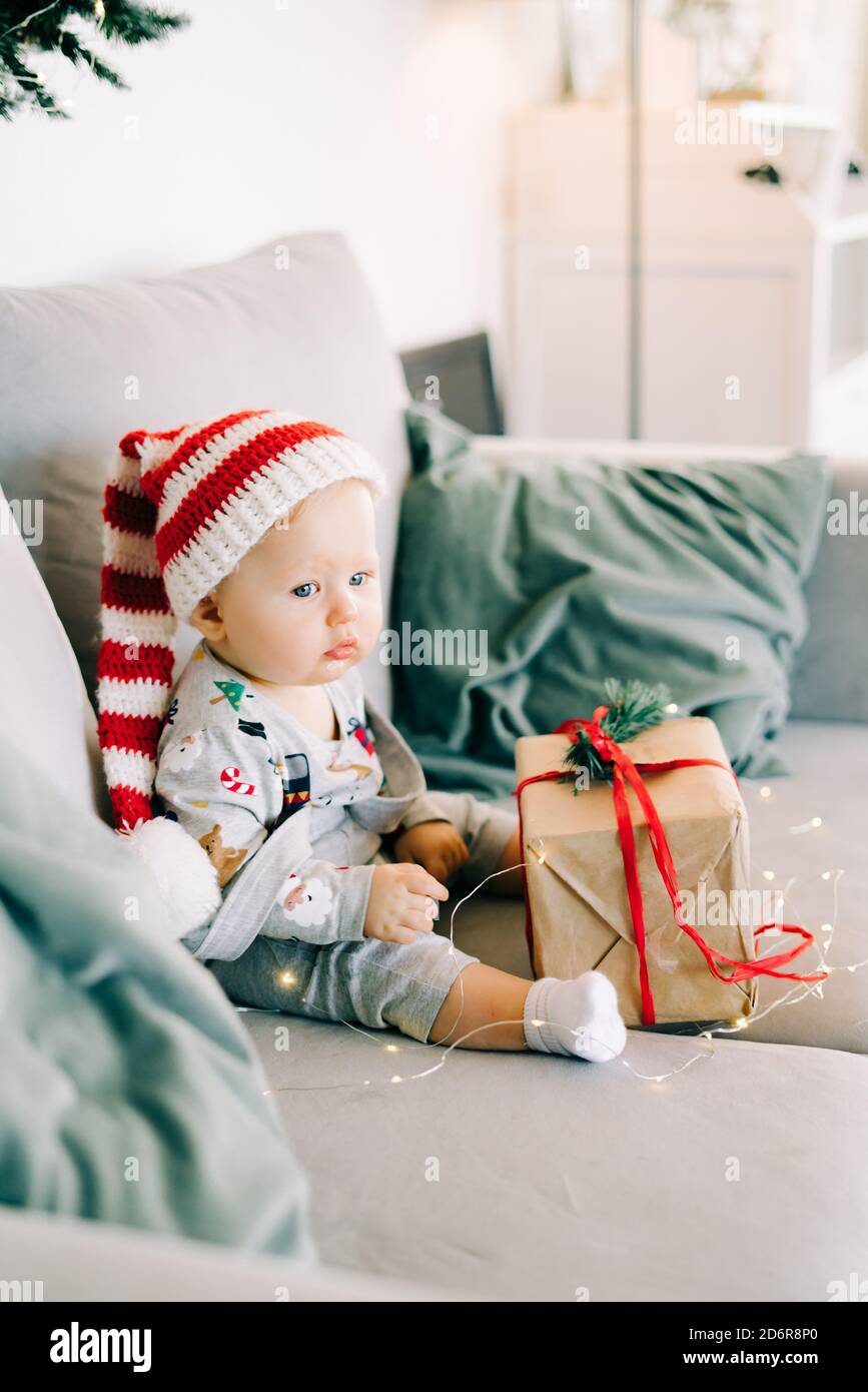 brooding little boy sits in Santa hat and holiday costume on gray sofa ...
