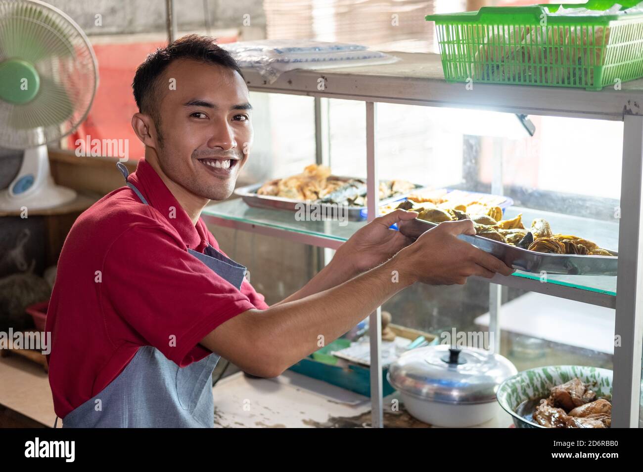 The food stall vendor smiles looking at the camera while holding the ...