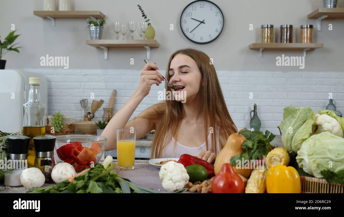 Happy cute young girl eating raw sprouts buckwheat with nuts in kitchen ...