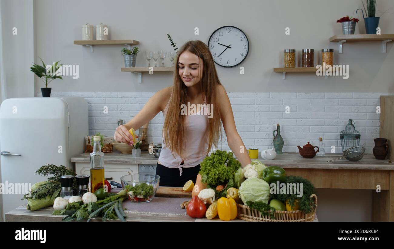 Cheerful vegan girl cooking salad with raw vegetables, adding lemon ...