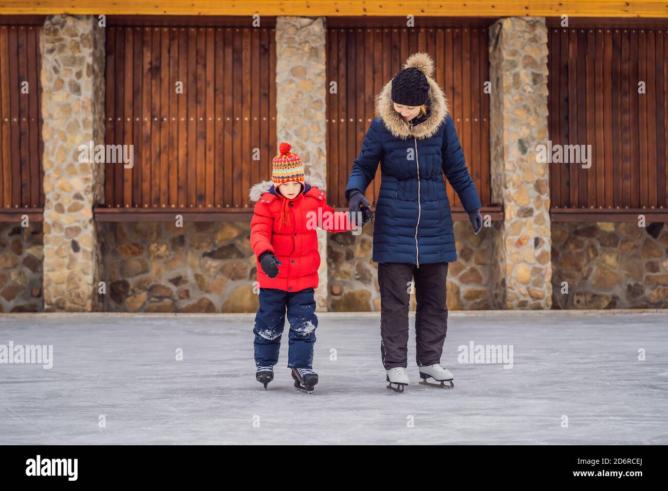 young mother teaching her little son ice skating at outdoor skating ...