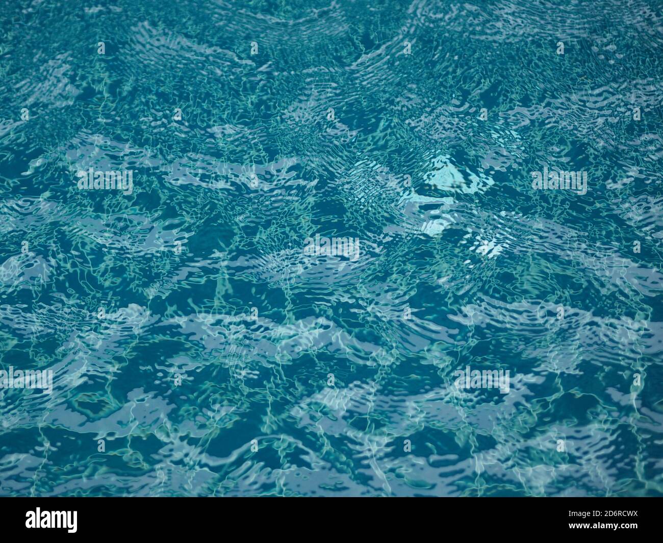 Rain drops falling blue water in pool background ripples on the surface texture, glittering ...