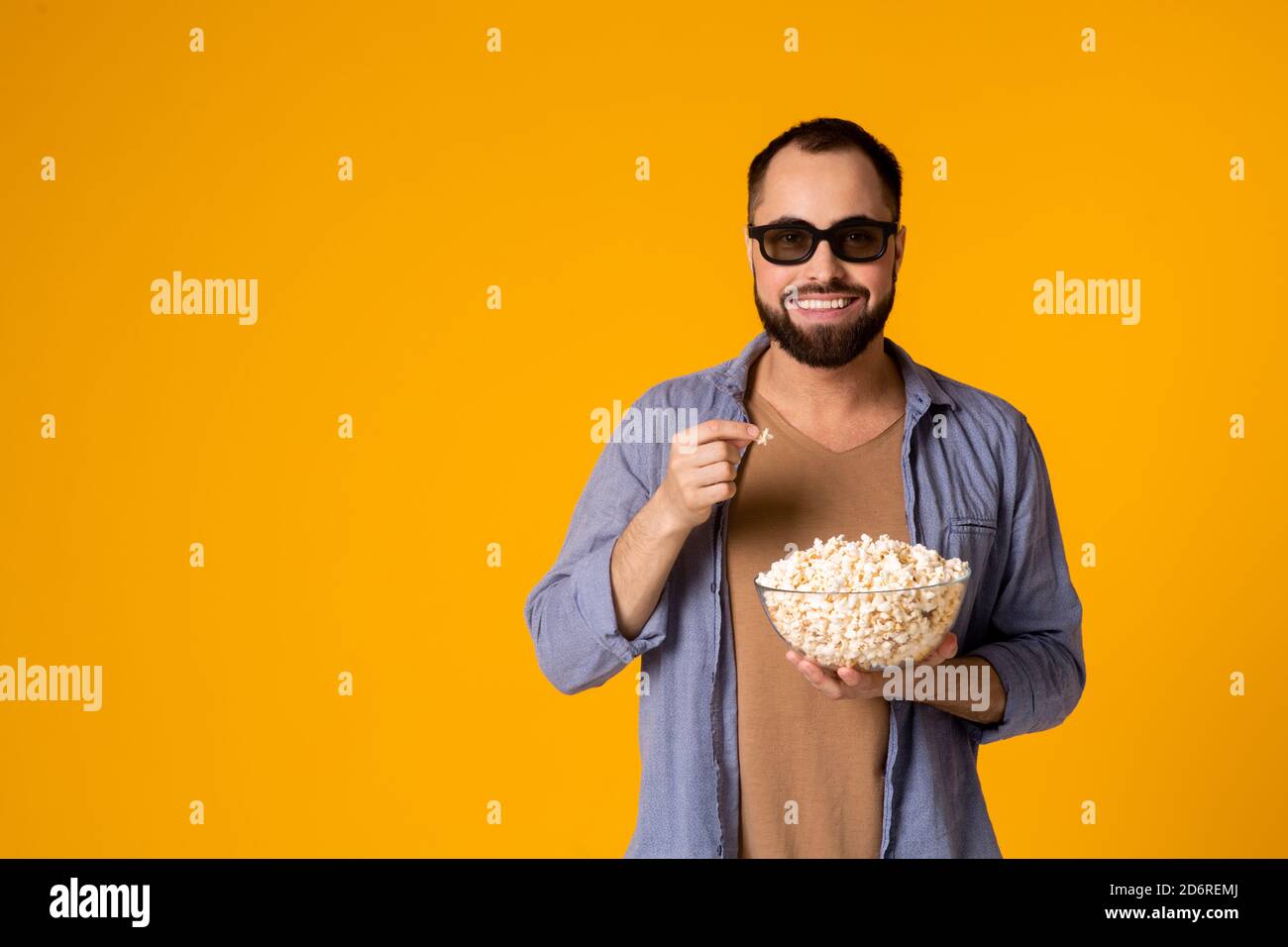 mage of a laughing emotional pleased young man in casual blue shirt eat popcorn wearing 3d ...
