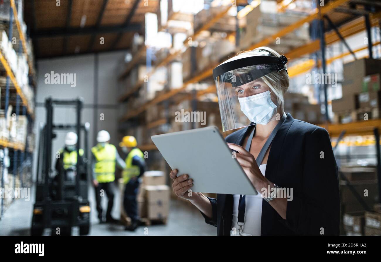 Manager with protective shield uisng tablet indoors in warehouse ...