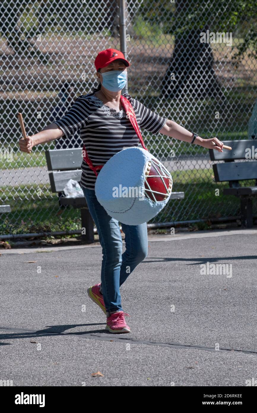 An Asian American member of a drum ensemble rehearses in a park in ...