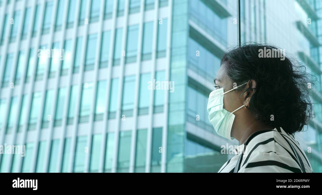 Side view of businesswoman with face mask on, looking to high rise ...