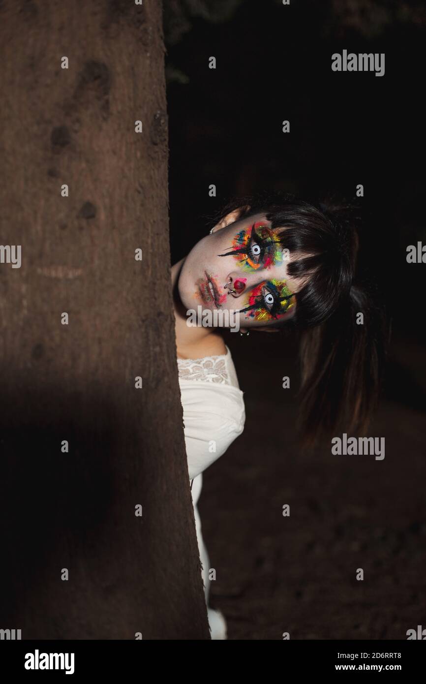 Creepy female with creative makeup and in contact lenses standing near ...