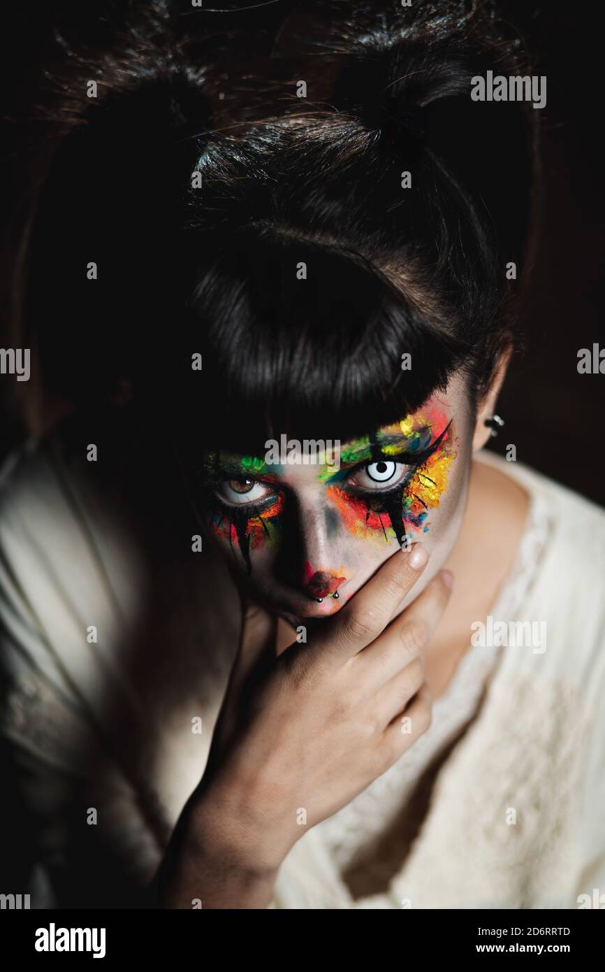 Scary young female in colorful contact lenses and with painted face ...