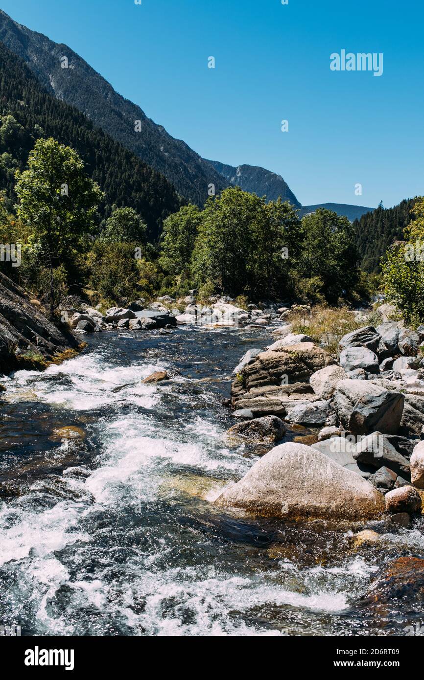 Long narrow waterfall of mountain river flowing over big stones between ...