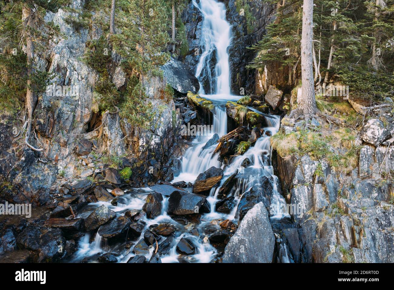 Long narrow waterfall of mountain river flowing over big stones between ...