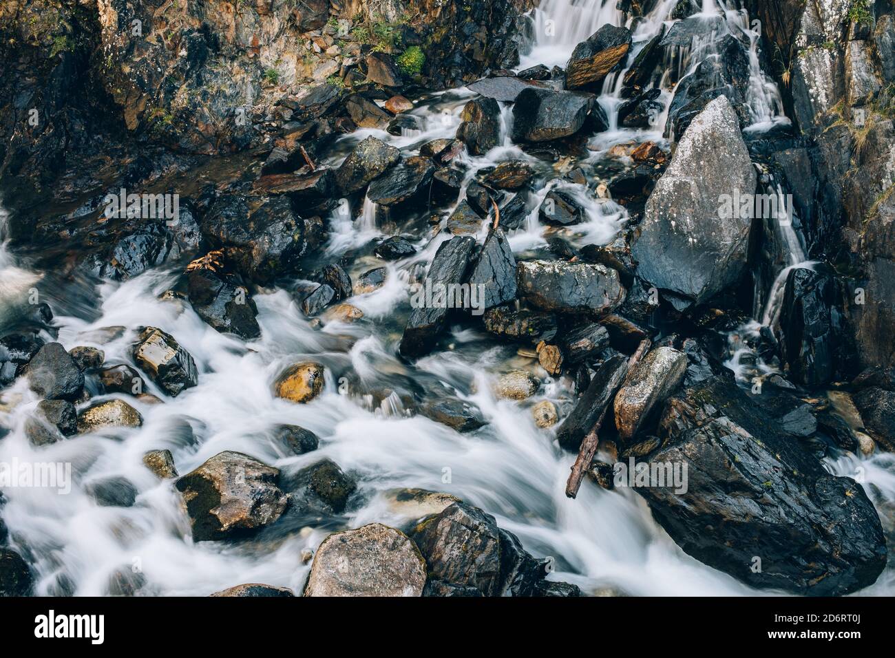 Long narrow waterfall of mountain river flowing over big stones between ...