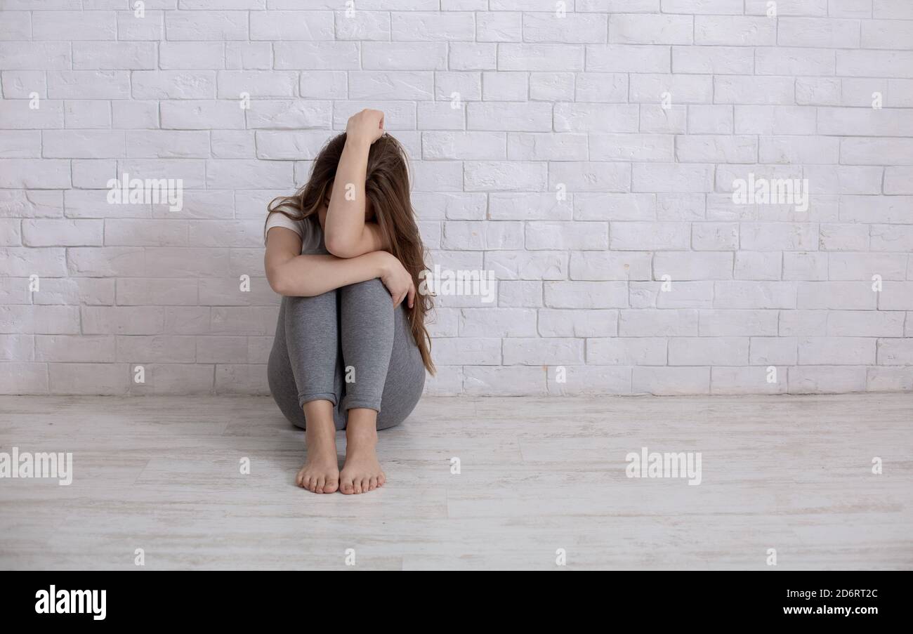 Desperate young lady crying from hopelessness on floor near white wall ...