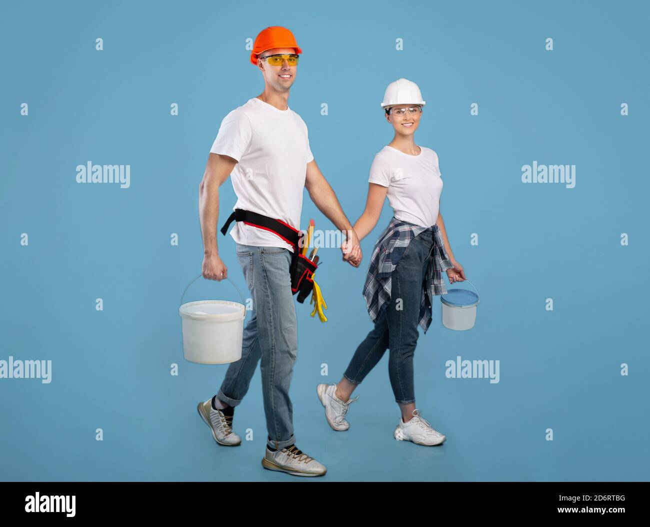 Smiling couple of painters holding hands walking with paint buckets ...