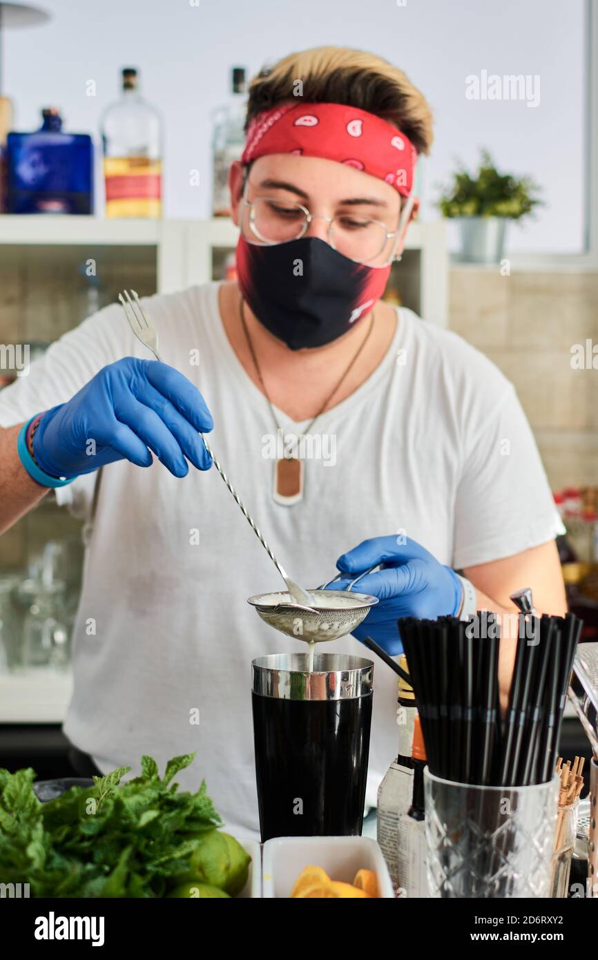 Male barkeeper in mask and gloves pouring milk into shaker while ...
