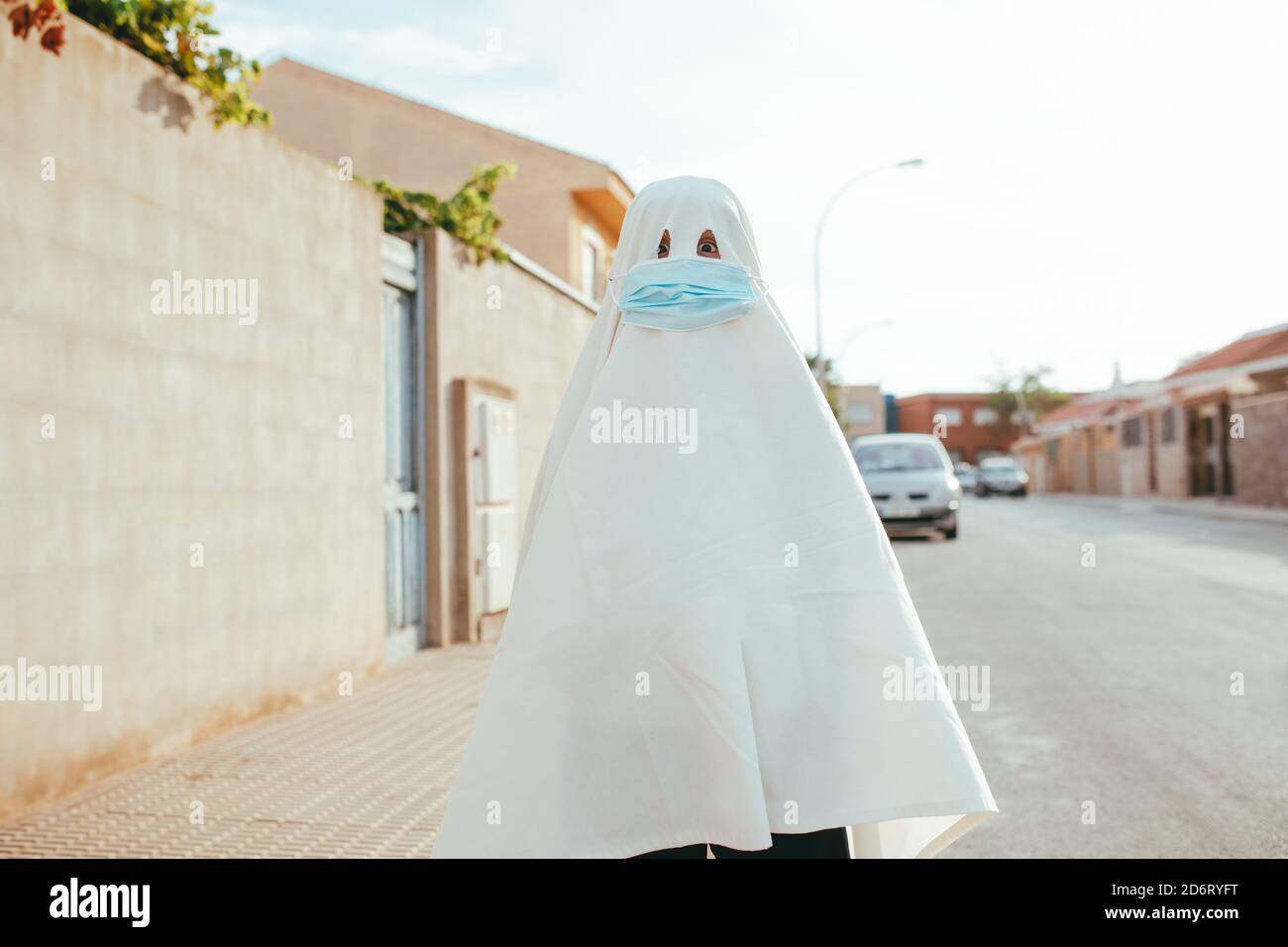 Anonymous spooky person wearing white ghost costume and medical mask ...