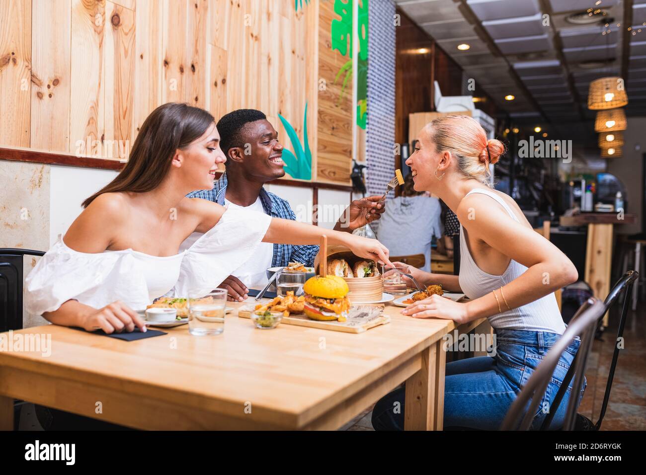 Positive young multiracial friends eating tasty dishes and burgers ...