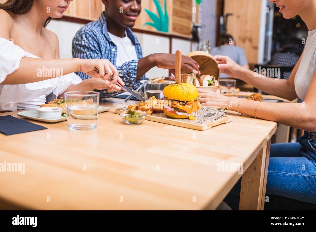 Positive young multiracial friends eating tasty dishes and burgers ...