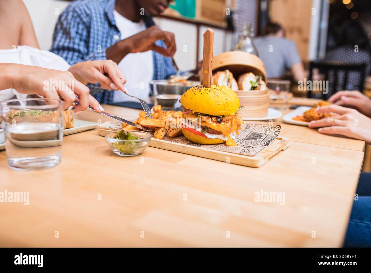 Positive young multiracial friends eating tasty dishes and burgers ...