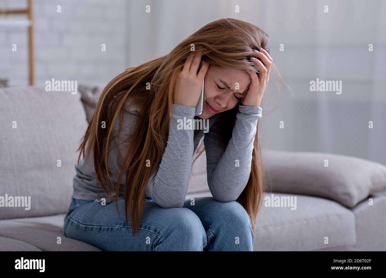 Sad young woman having conversation on mobile phone and crying at home ...