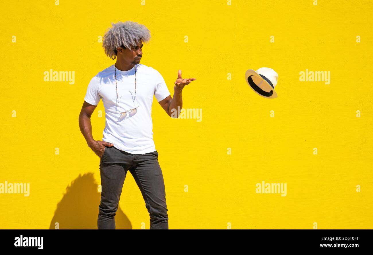 Black man with afro hair throwing a straw hat on a yellow background ...