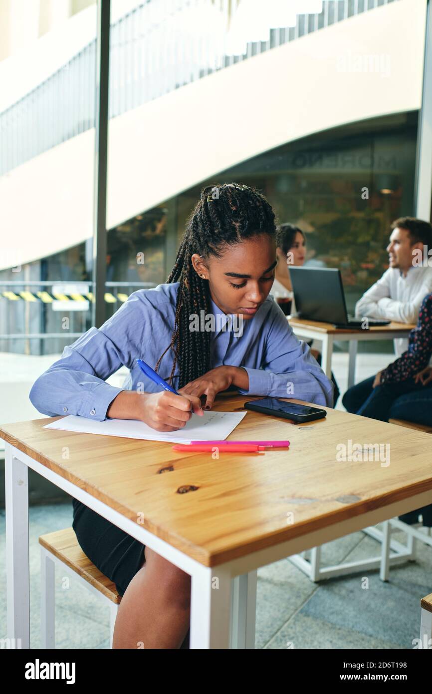 Young Woman with Afro braids writing with pen on paper while working on ...