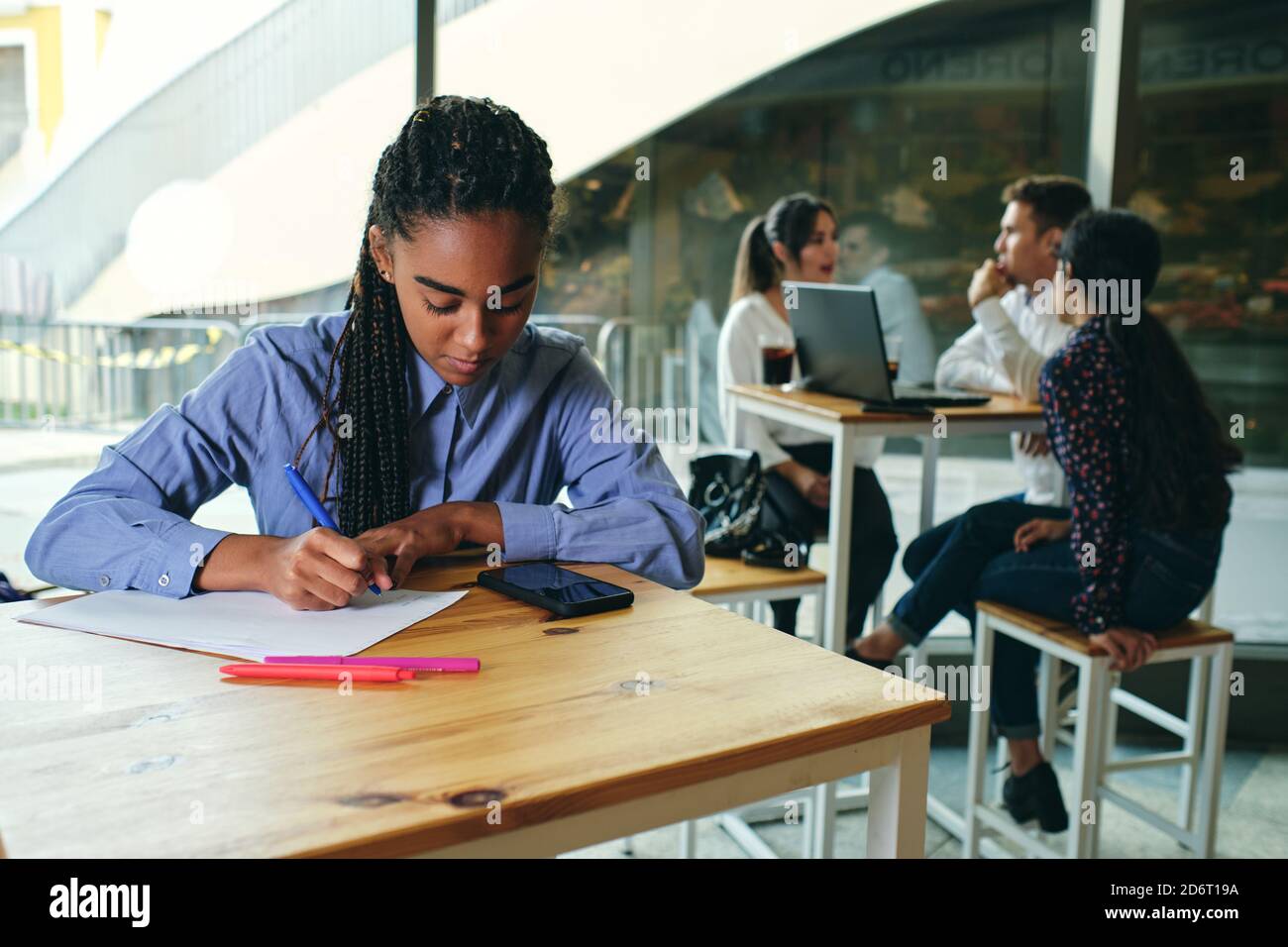 Young Woman with Afro braids writing with pen on paper while working on ...
