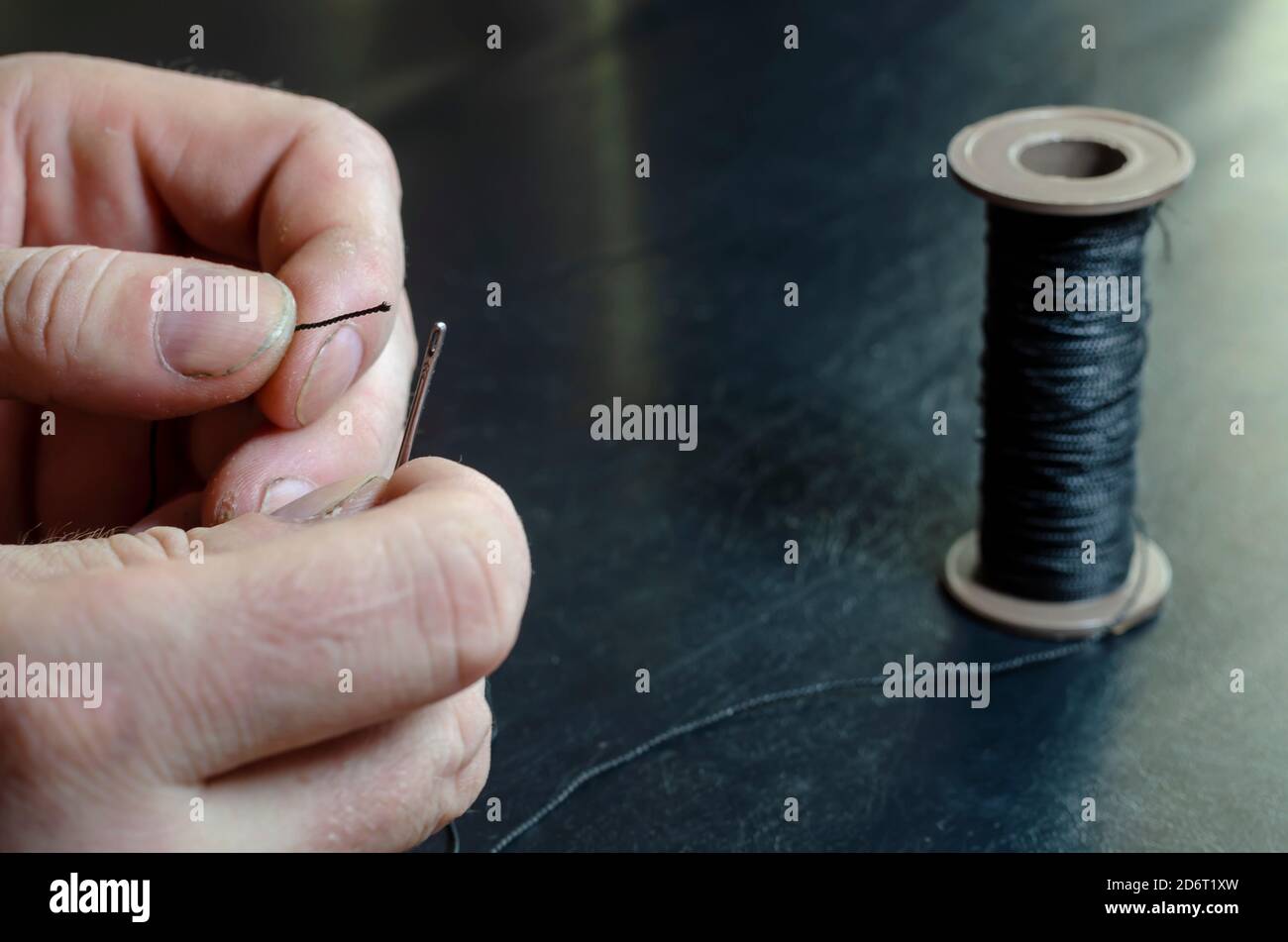 The man inserts the thread into the eye of the needle. Hands of an ...