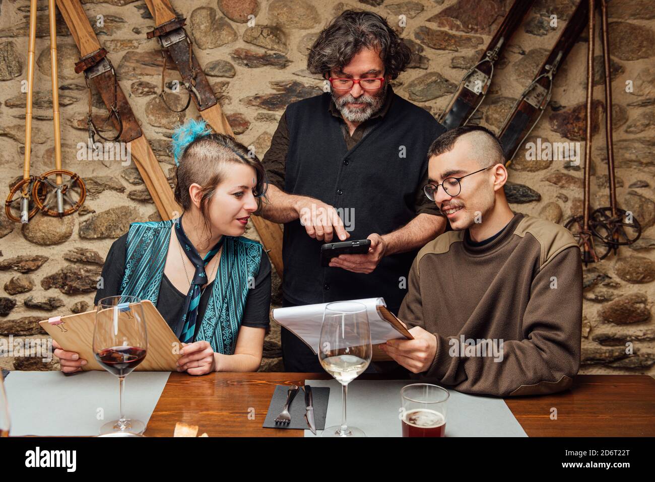 Cheerful couple of hipsters sitting at wooden table with menu and ...