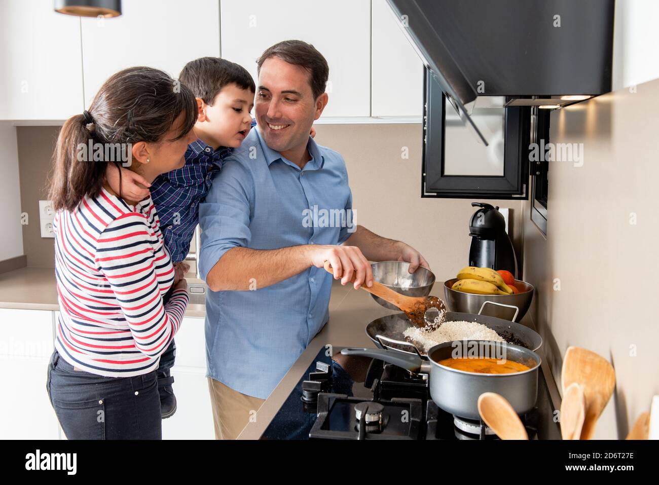 Cheerful family standing near stove and cooking rice for lunch while ...