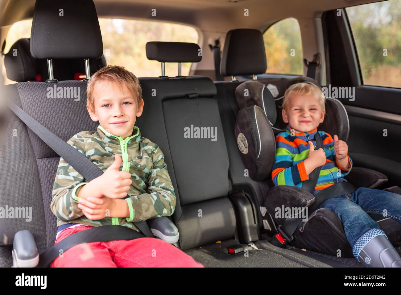 Two little boys sitting on a car seat and a booster seat buckled up in ...