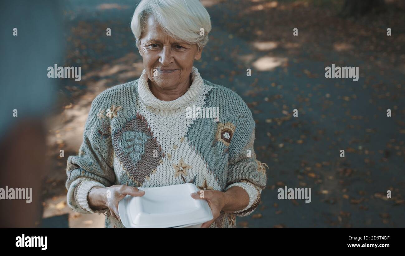 Old vulnerable homeless woman getting free charity meal. High quality ...