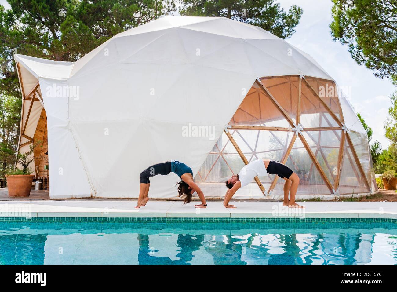 Slim partners in sportswear standing in bridge na pose while practicing ...