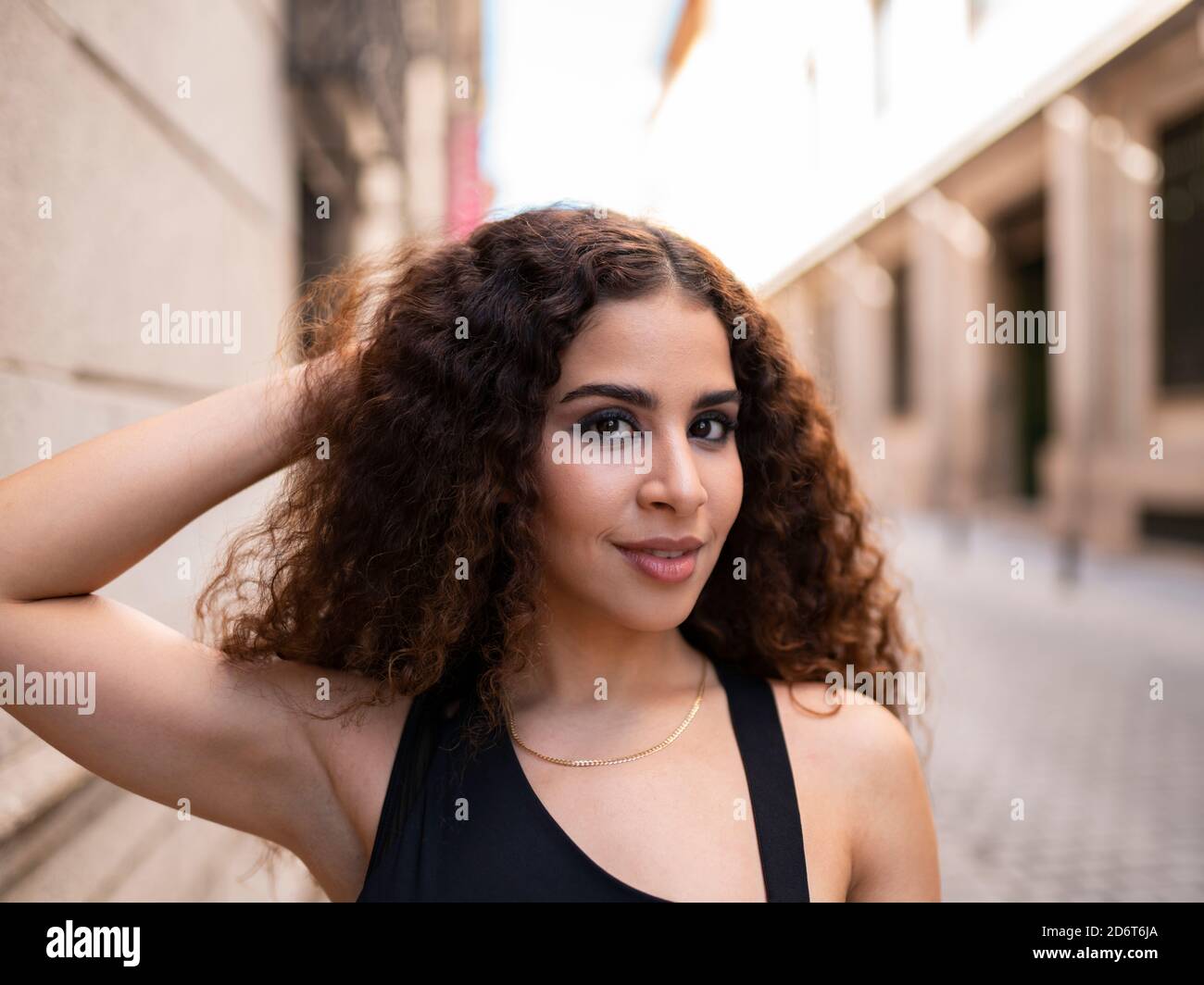Self assured young ethnic female with long curly hair touching hair ...