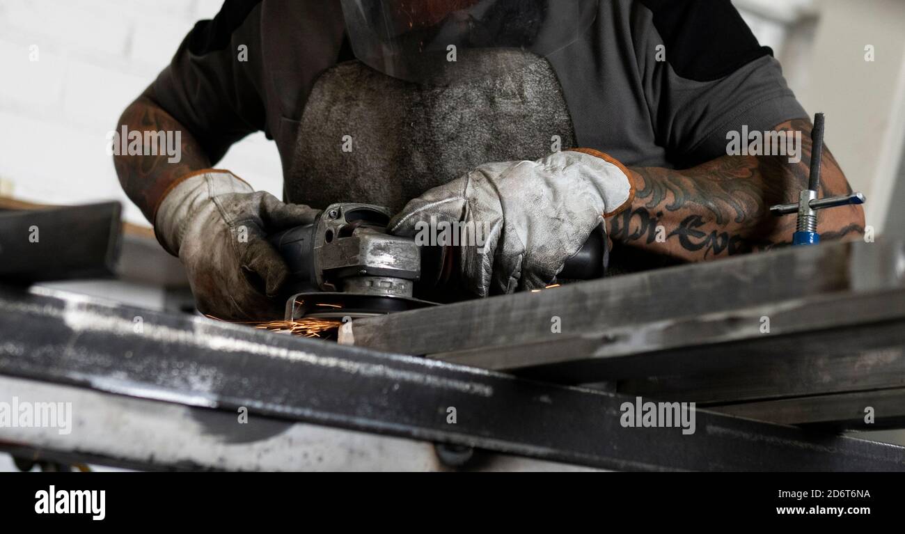 Side view of male welder using electric grinder and cutting metal ...