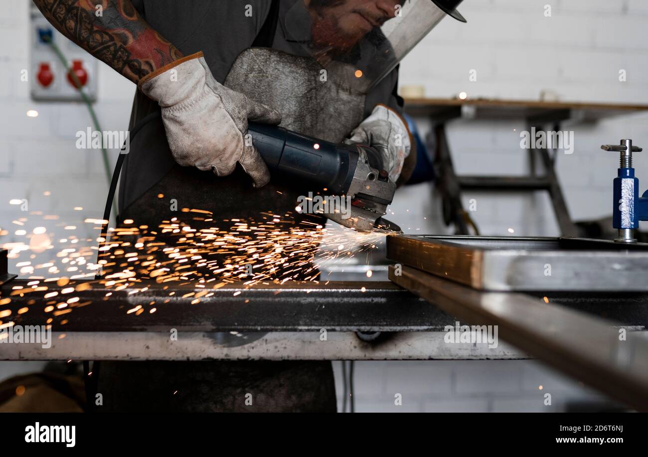 Side view of serious male welder using electric grinder and cutting ...
