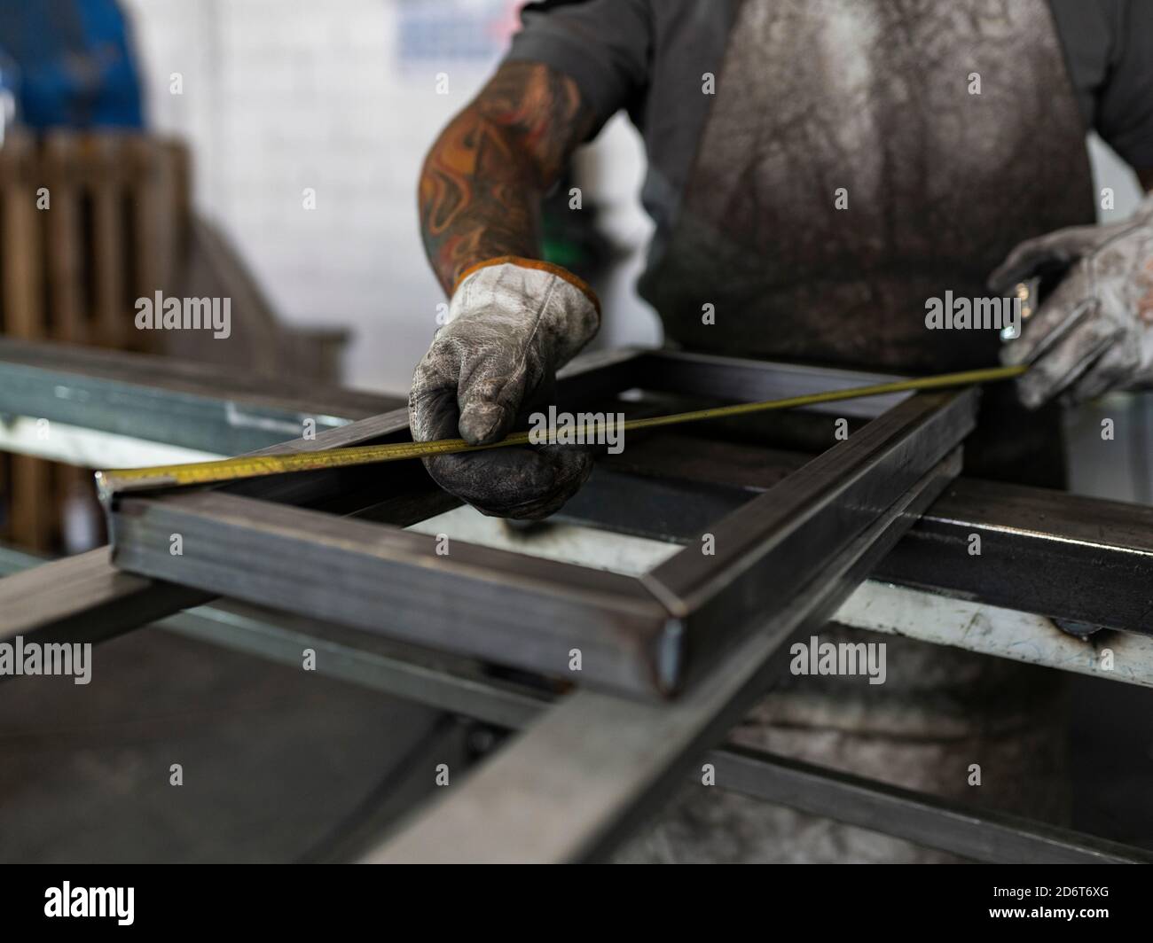 Unrecognizable male welder in dirty gloves and apron measuring frame ...