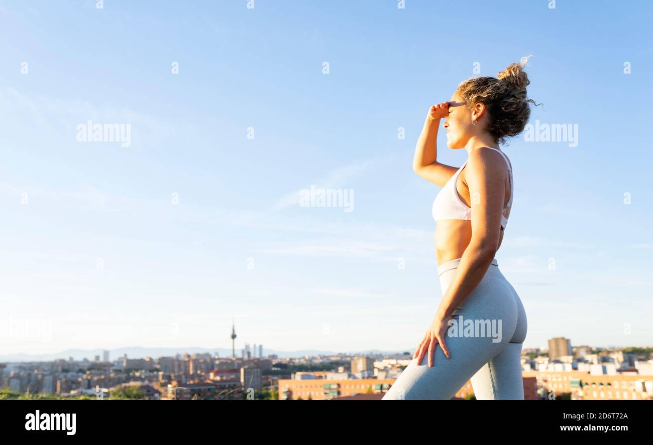 Side view sporty female in leggings and sports bra hiding eyes from sun ...