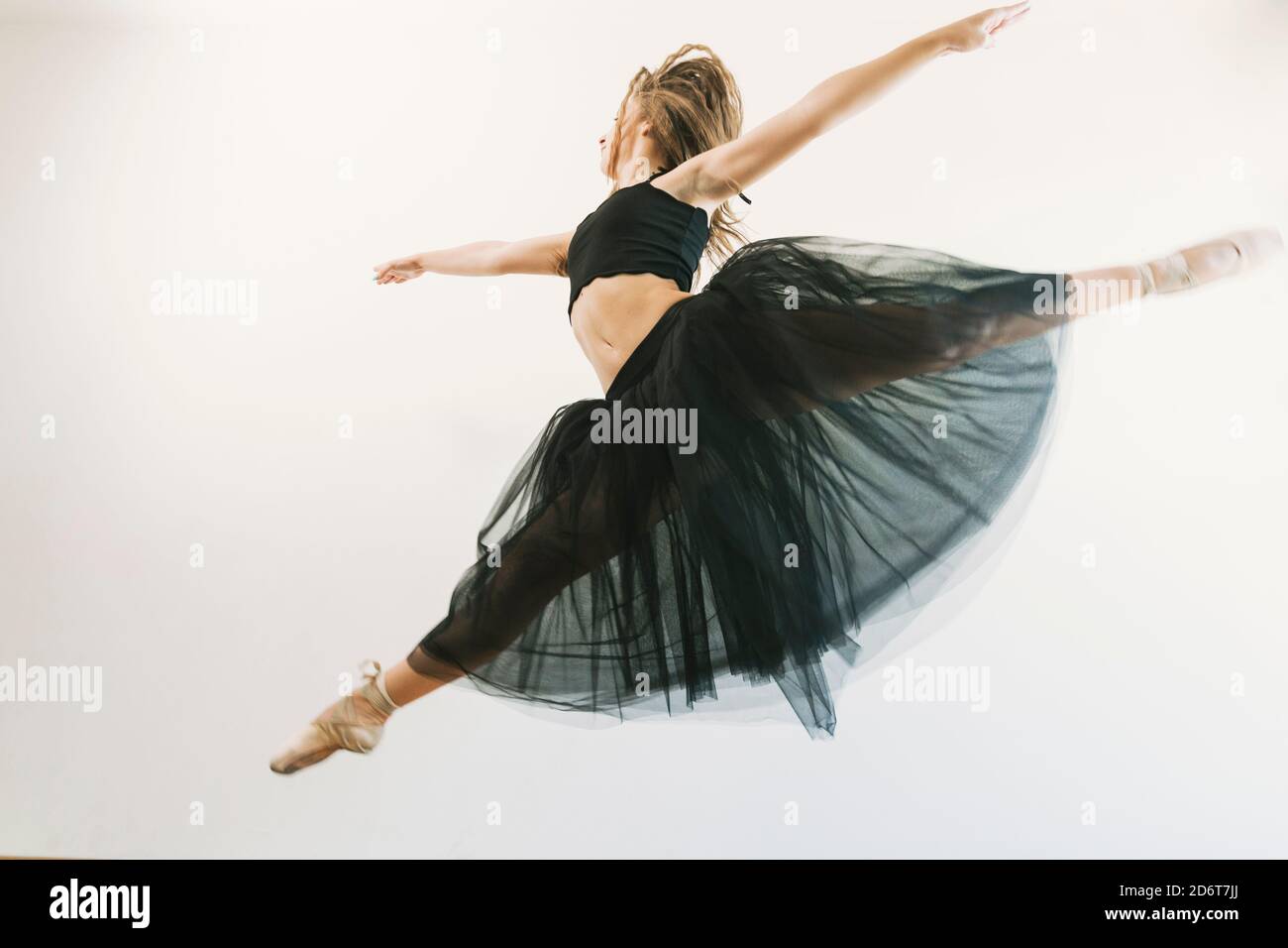 Side view of ballerina in black tutu jumping in splits with ...