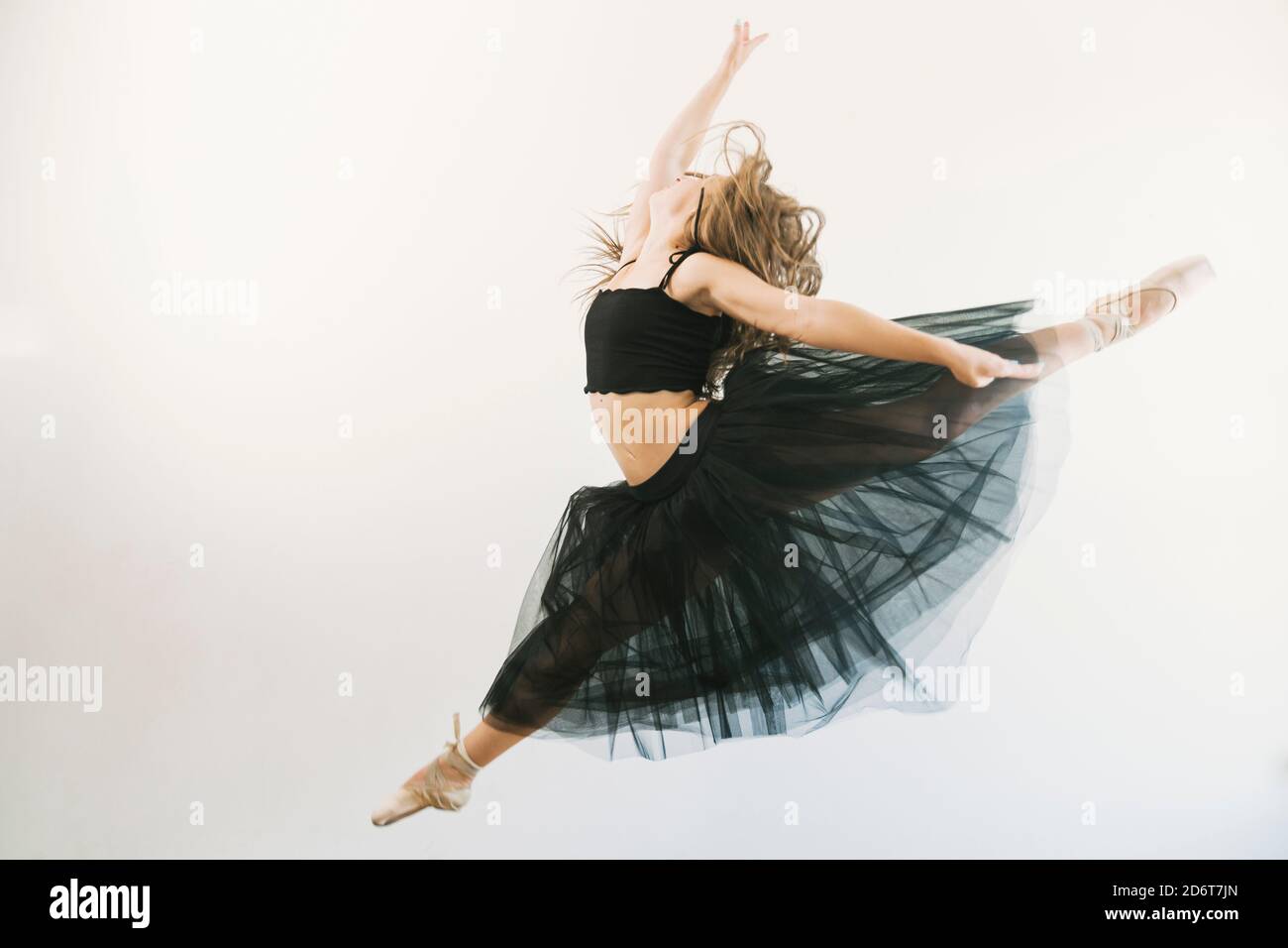 Side view of ballerina in black tutu jumping in splits with ...