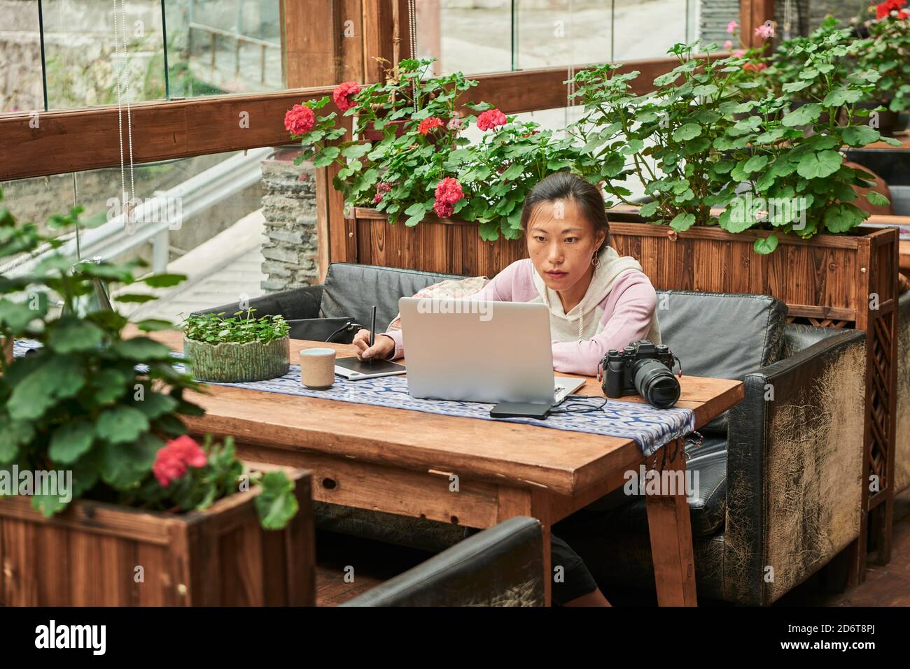 Concentrated Asian female journalist sitting at table with digital ...