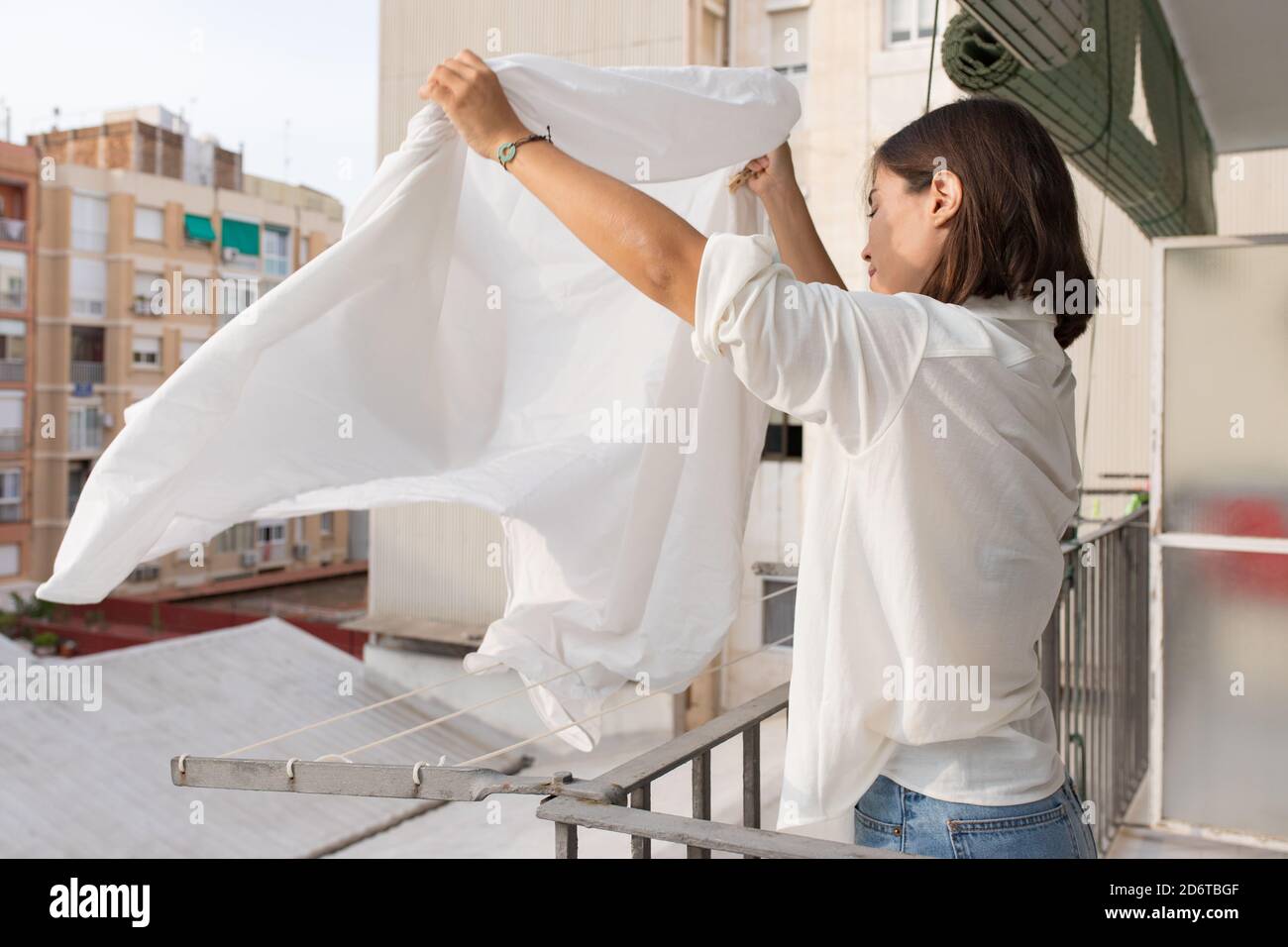 Side view of young female in white shirt and jeans hanging laundry on ...