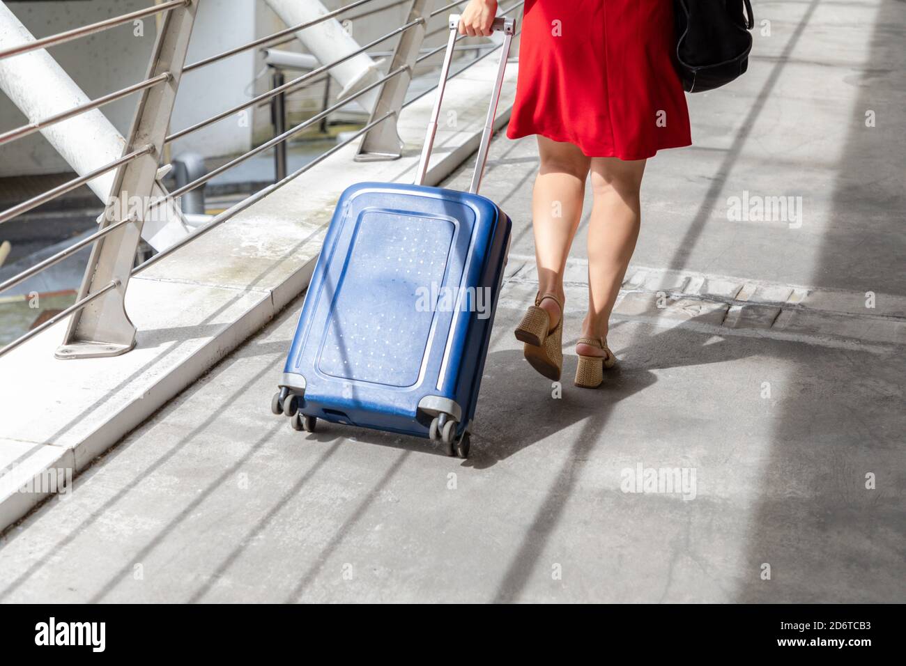Crop of back view of anonymous Woman in red dress walking with suitcase ...