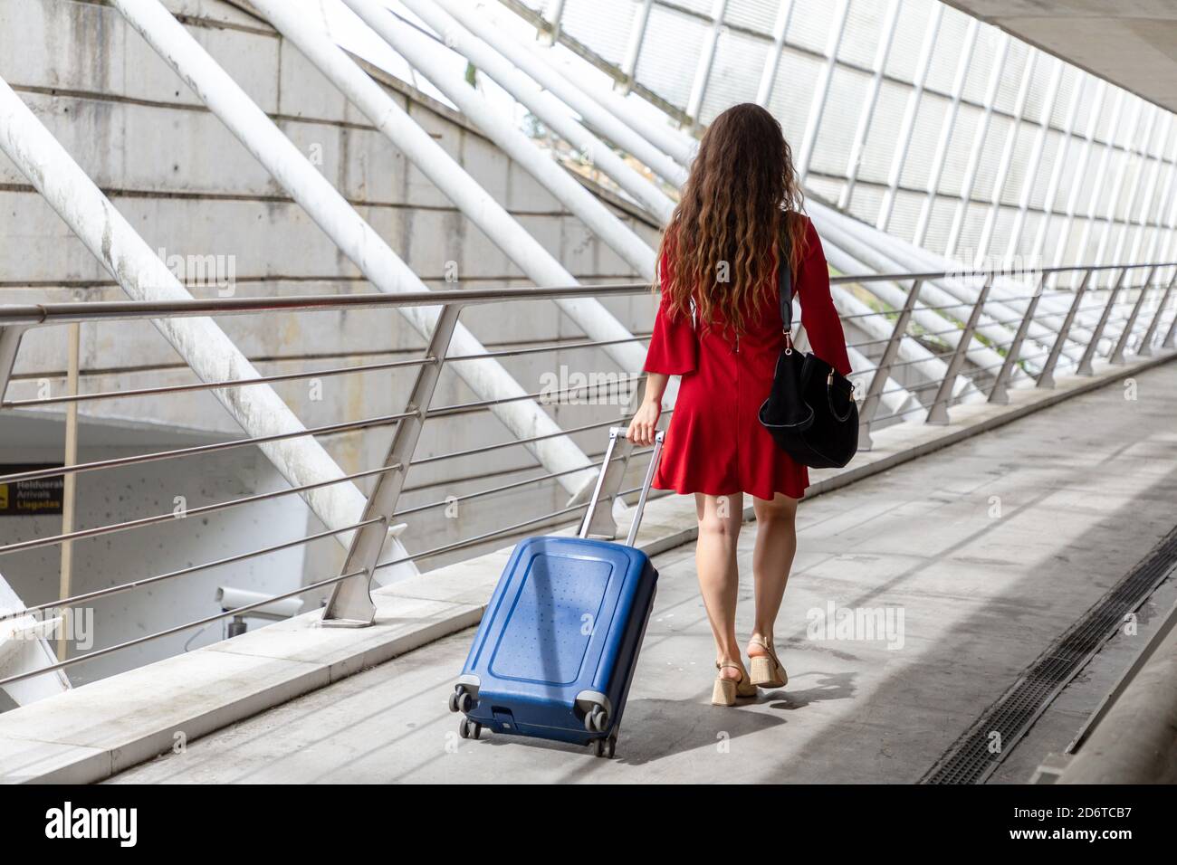 Back view of anonymous Woman in red dress walking with suitcase in ...