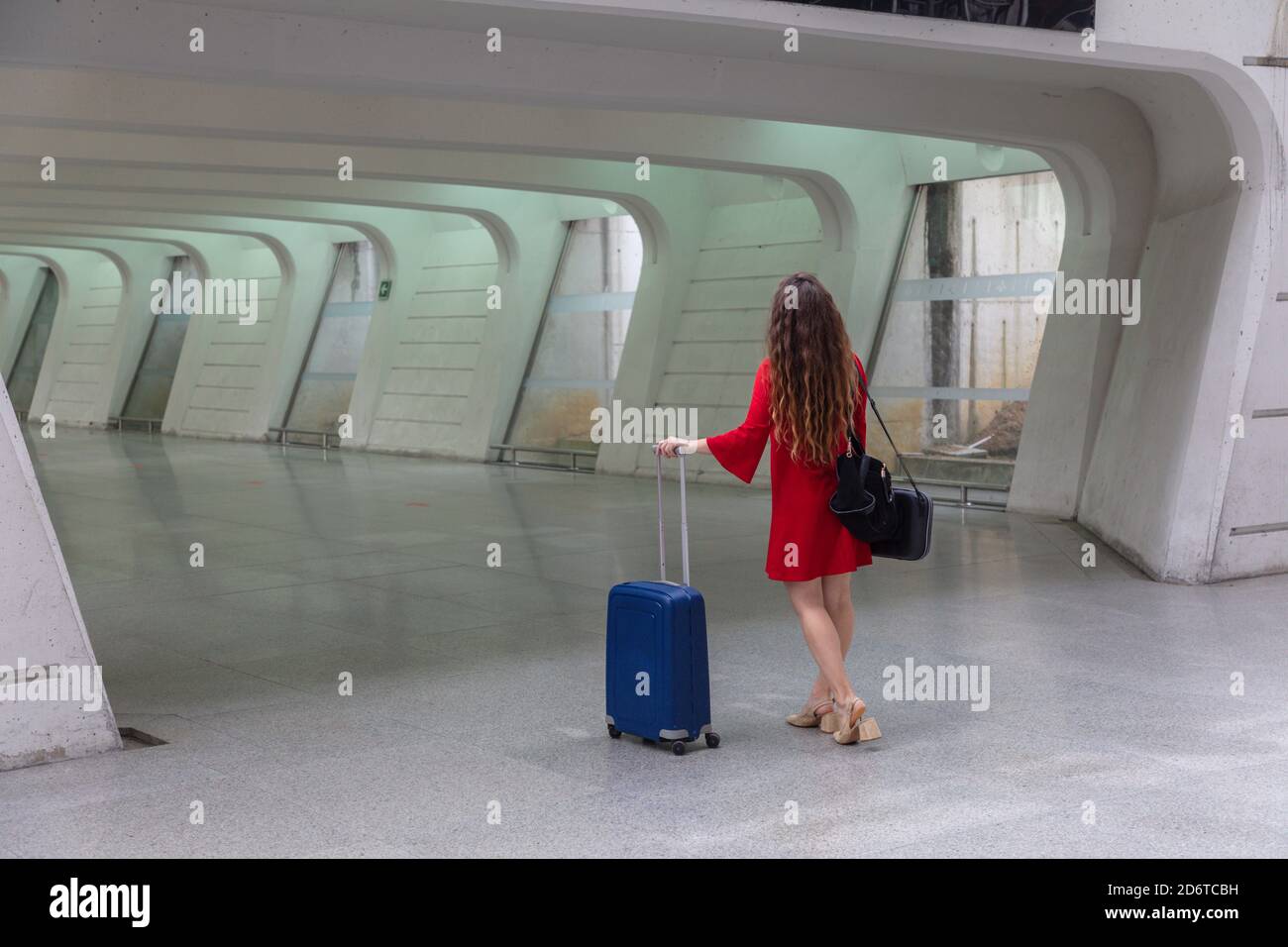 Back view of anonymous Woman in red dress walking with suitcase in ...